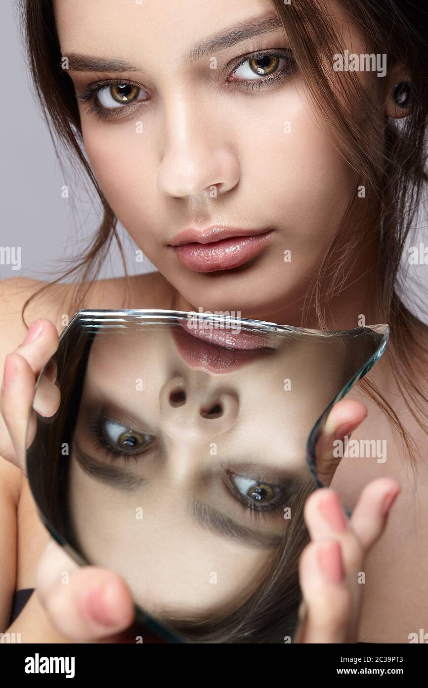 Female with mirror shard in hand posing on gray background. Face ...