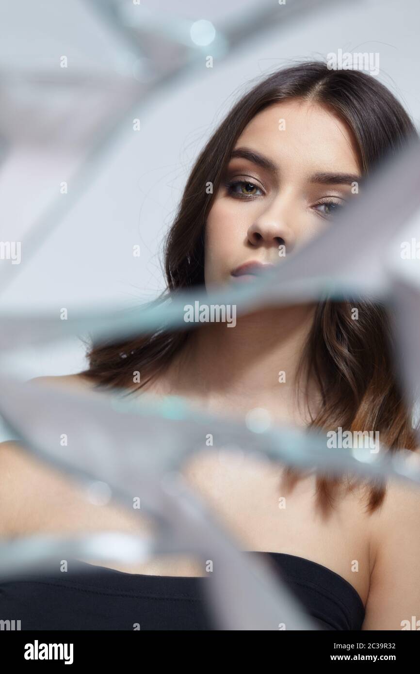 Young woman looks in a broken mirror. Portrait of beautiful female in ...
