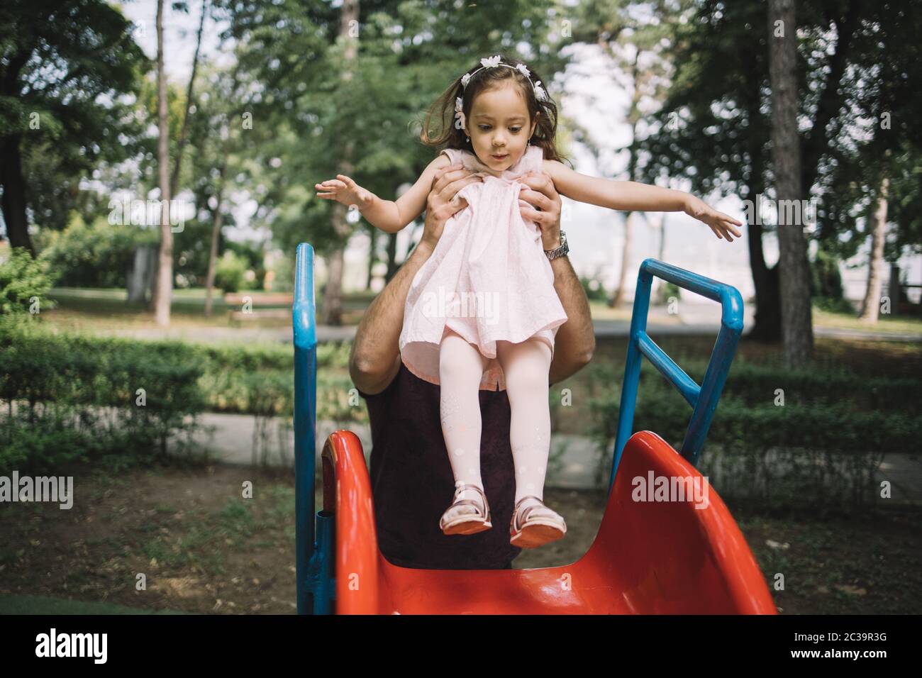 Man lifting little girl over slider in playground Stock Photo - Alamy