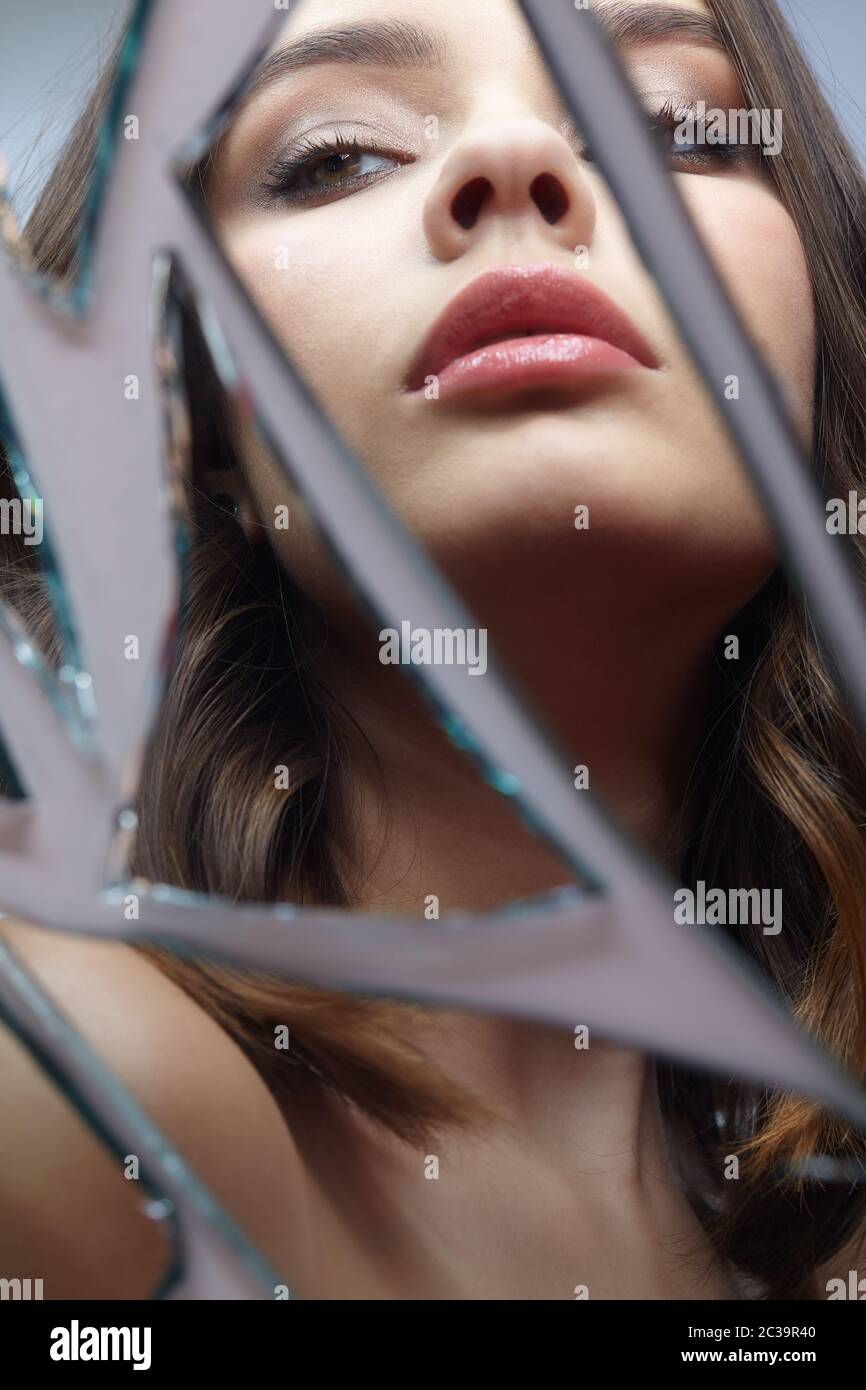 Young woman looks in a broken mirror. Portrait of beautiful female in ...