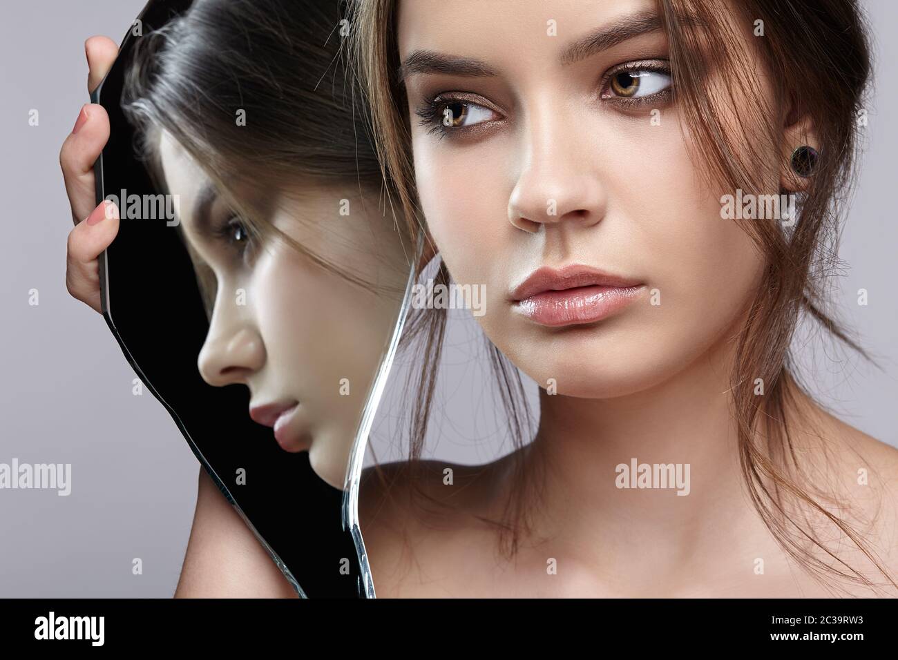 Female with mirror shard in hand posing on gray background. Face ...