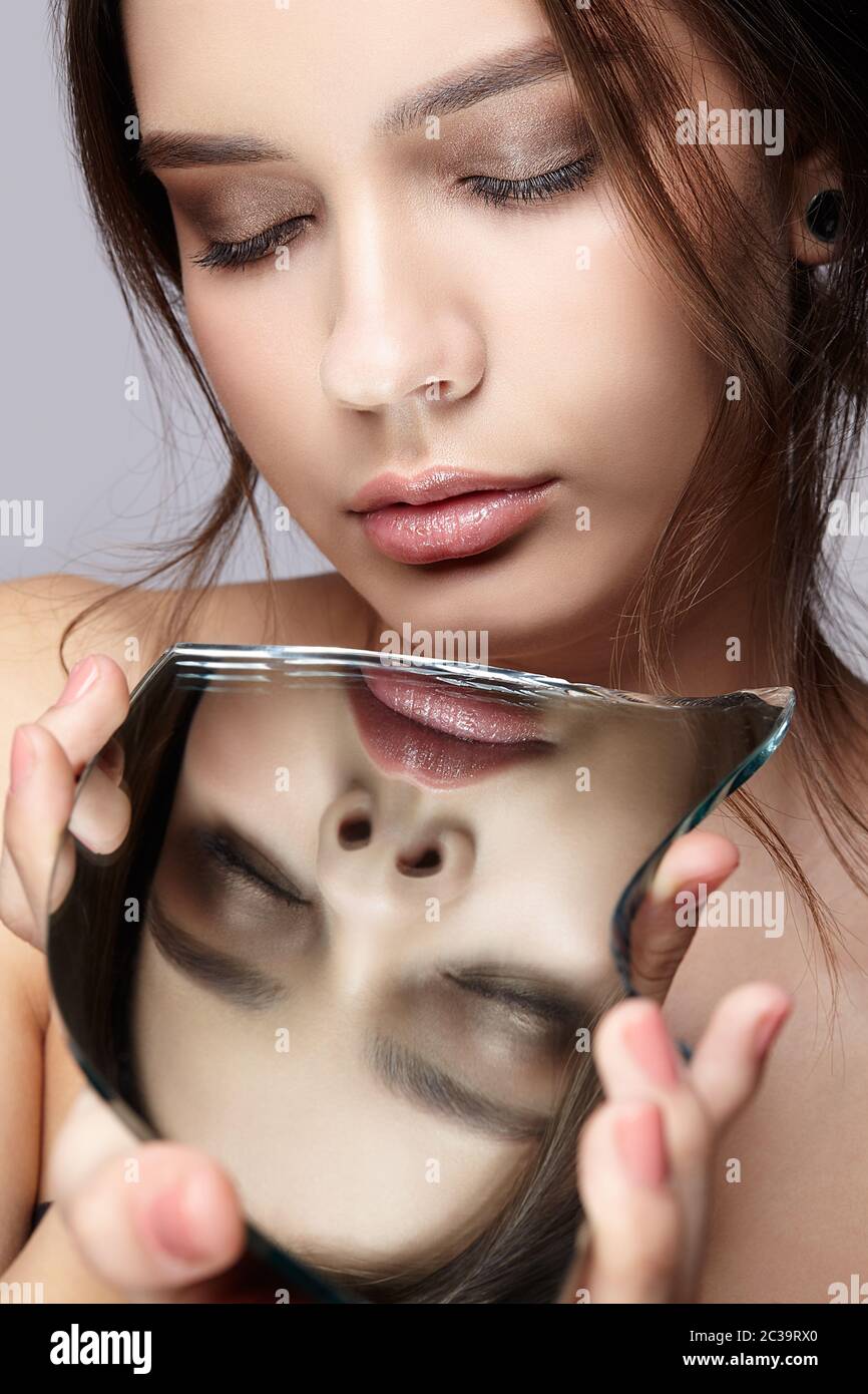 Female with mirror shard in hand posing on gray background. Face ...