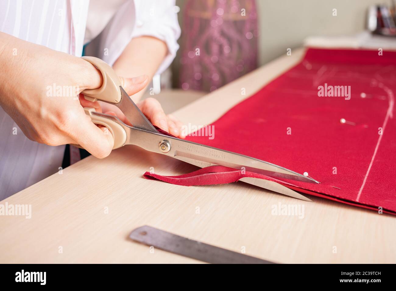 A seamstress woman cuts off the excess red fabric, the girl in the ...