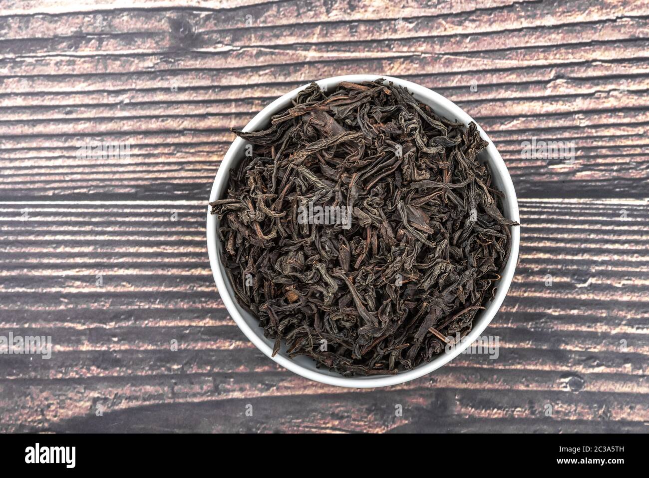 Dried tea is poured into a ceramic cup on a wooden plank table. View ...