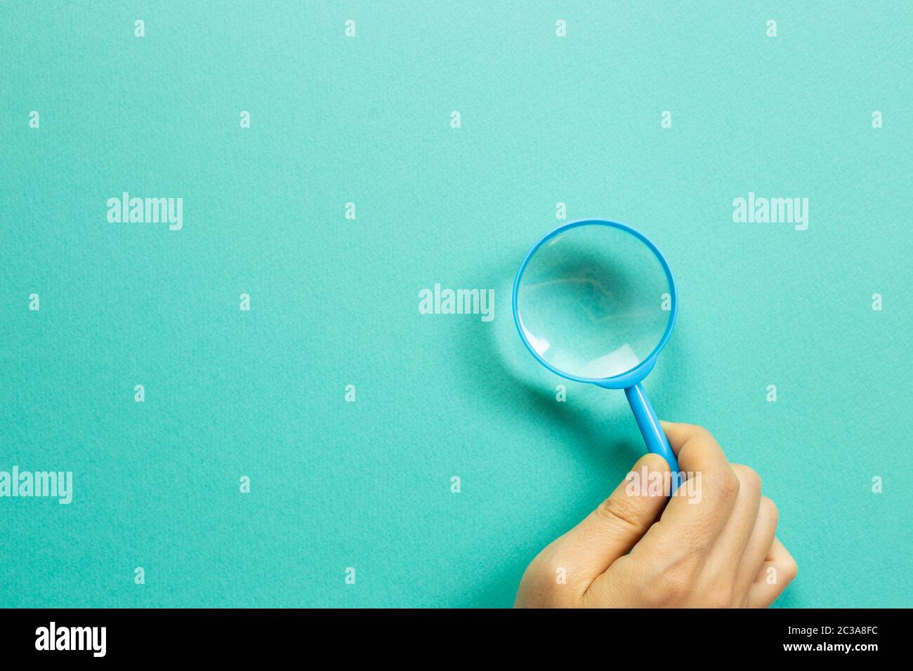Hand holding a blue magnifying glass on green background. top view ...