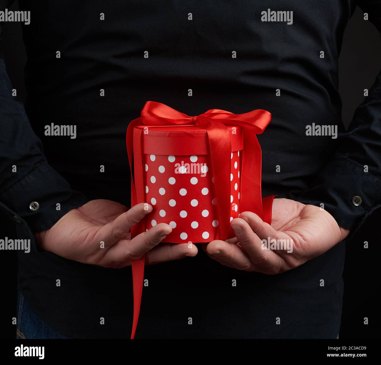 male hand holds a red paper box with a gift behind his back, man is ...