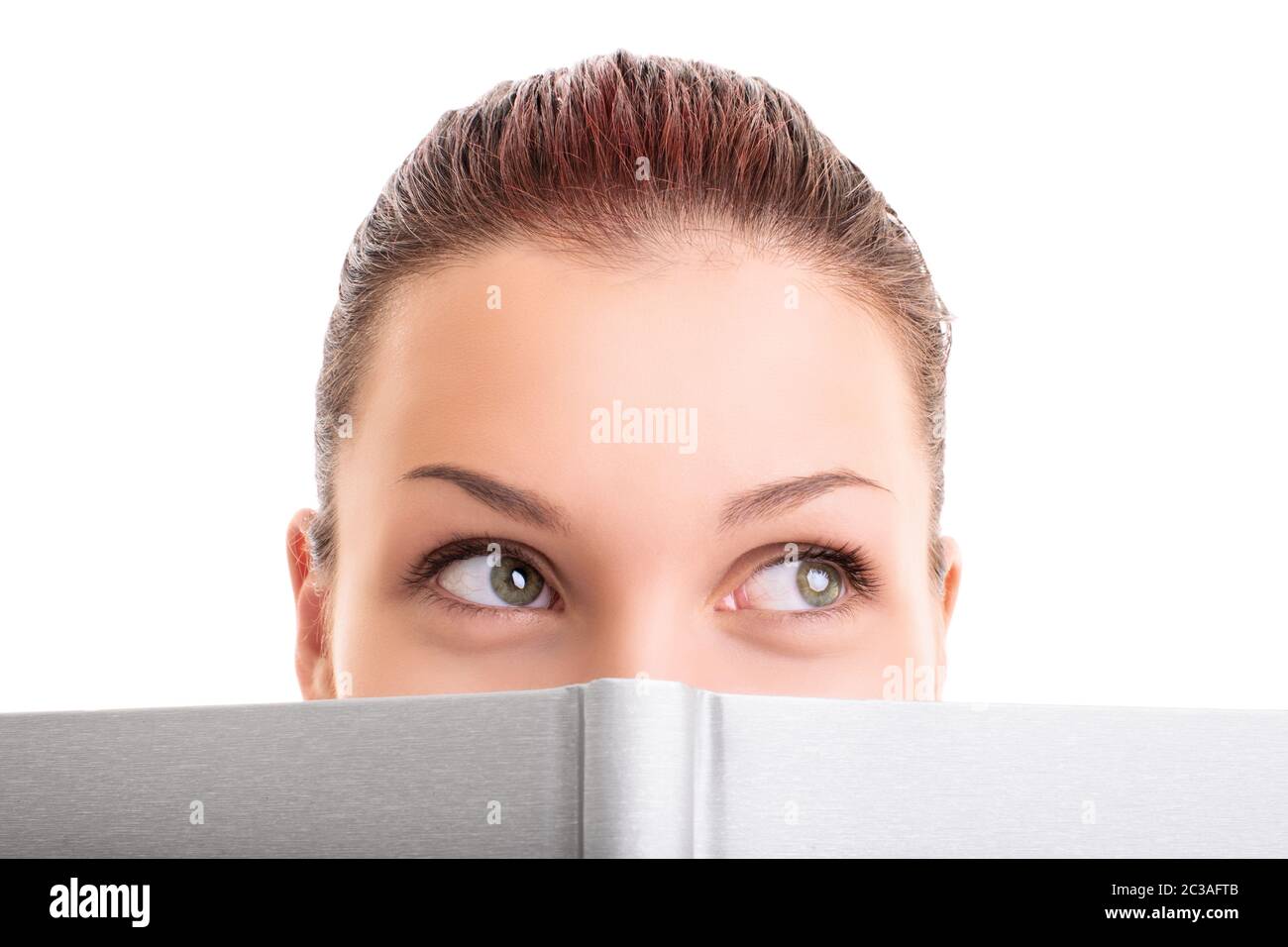 Close up shot of a pretty young girl hiding behind an open book looking ...