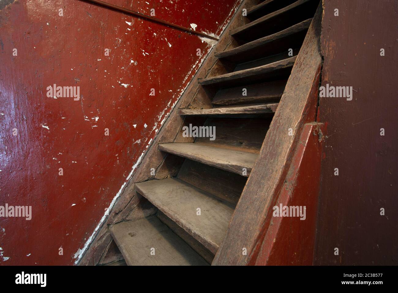 Old damaged brown wooden stairs and red wall leading to the attic ...