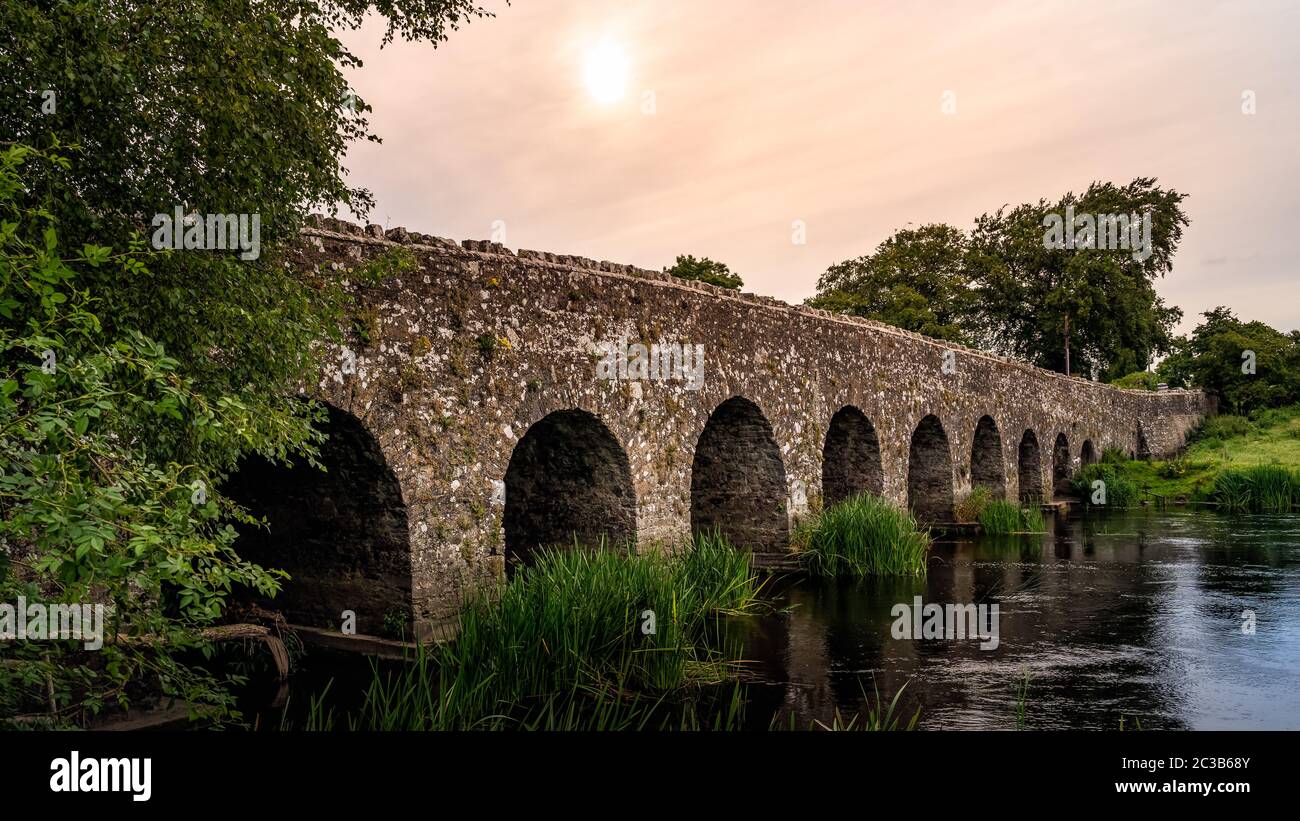 Old 12th century stone arch bridge over a river. Green fields and trees ...
