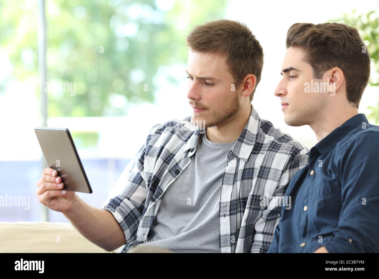 Two serious men checking tablet content sitting on a couch in the ...