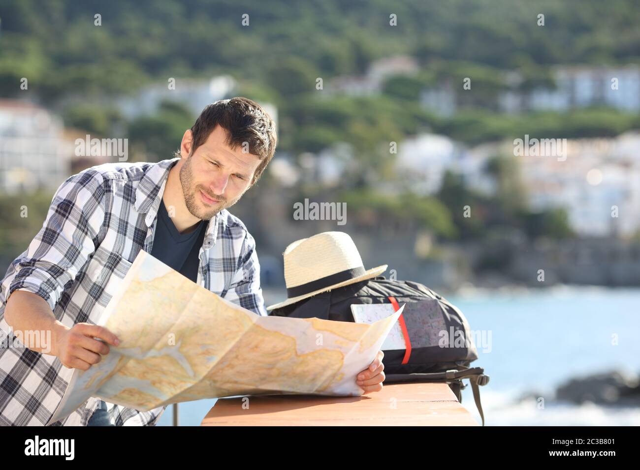 Serious tourist checking paper map traveling in a coast town on summer ...