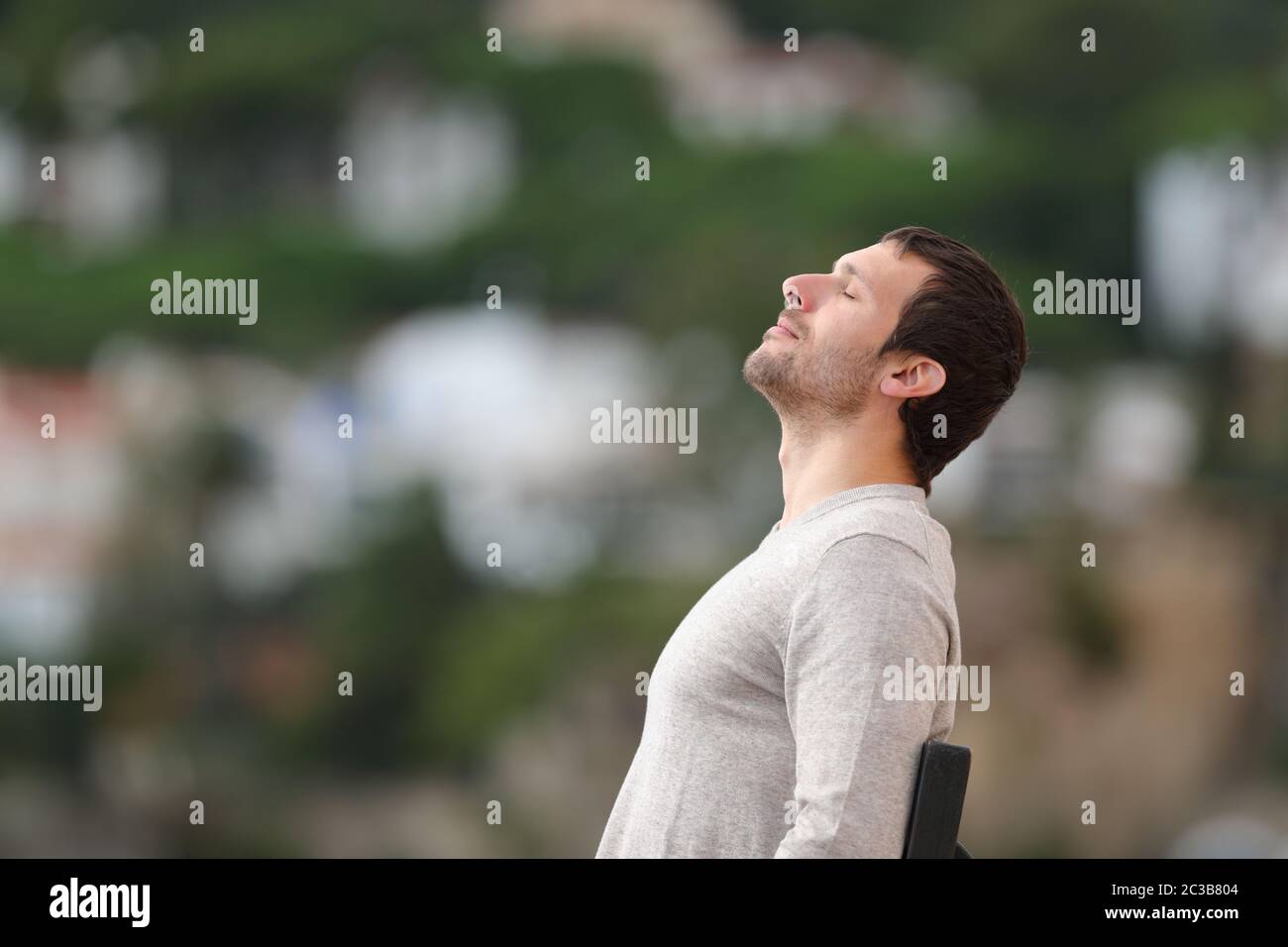 Side view portrait of a relaxed man sitting on a bench breathing fresh ...