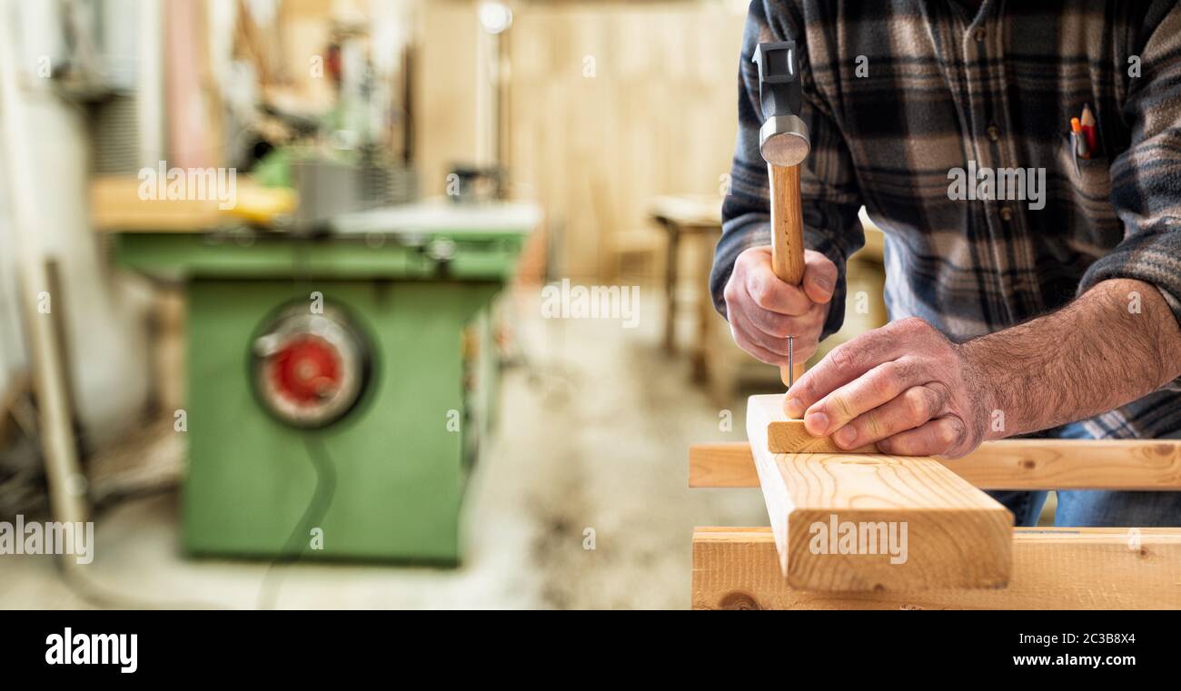 Close-up. Carpenter with hammer and nails fixes a wooden board ...