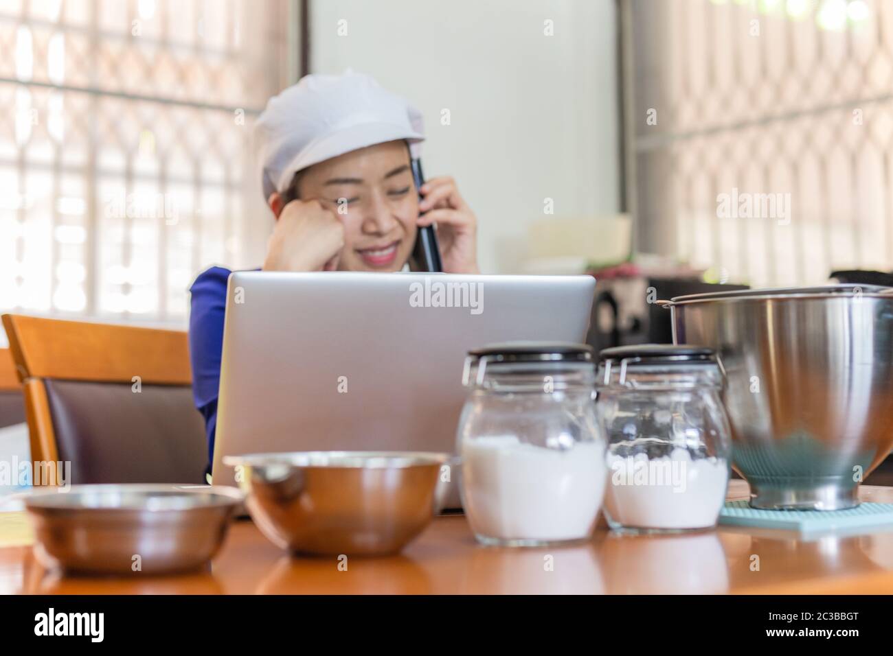 Happy woman baker talking on cell phone with laptop and bakery ...