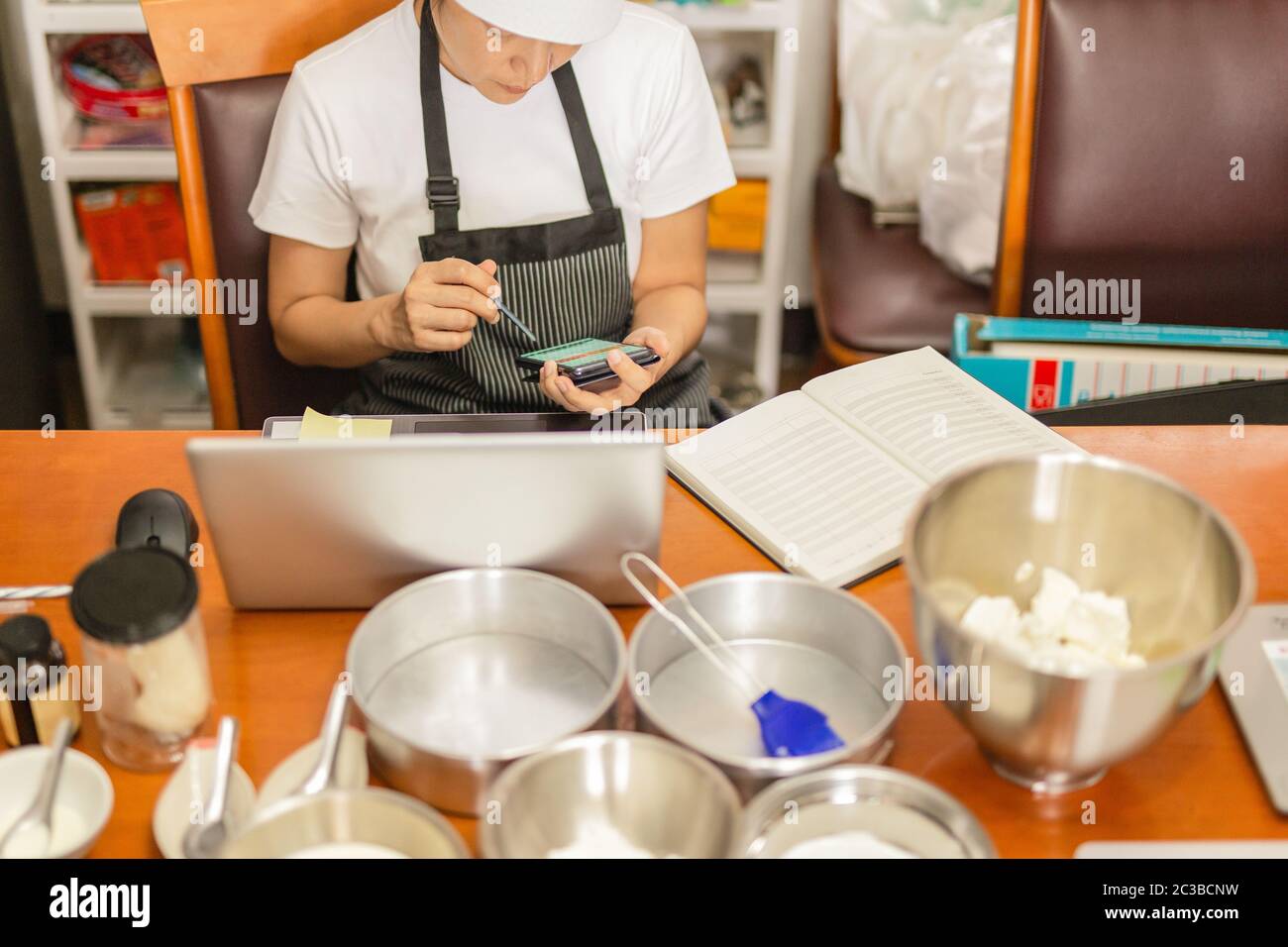 Female baker using cell phone with laptop and bakery ingredient on ...