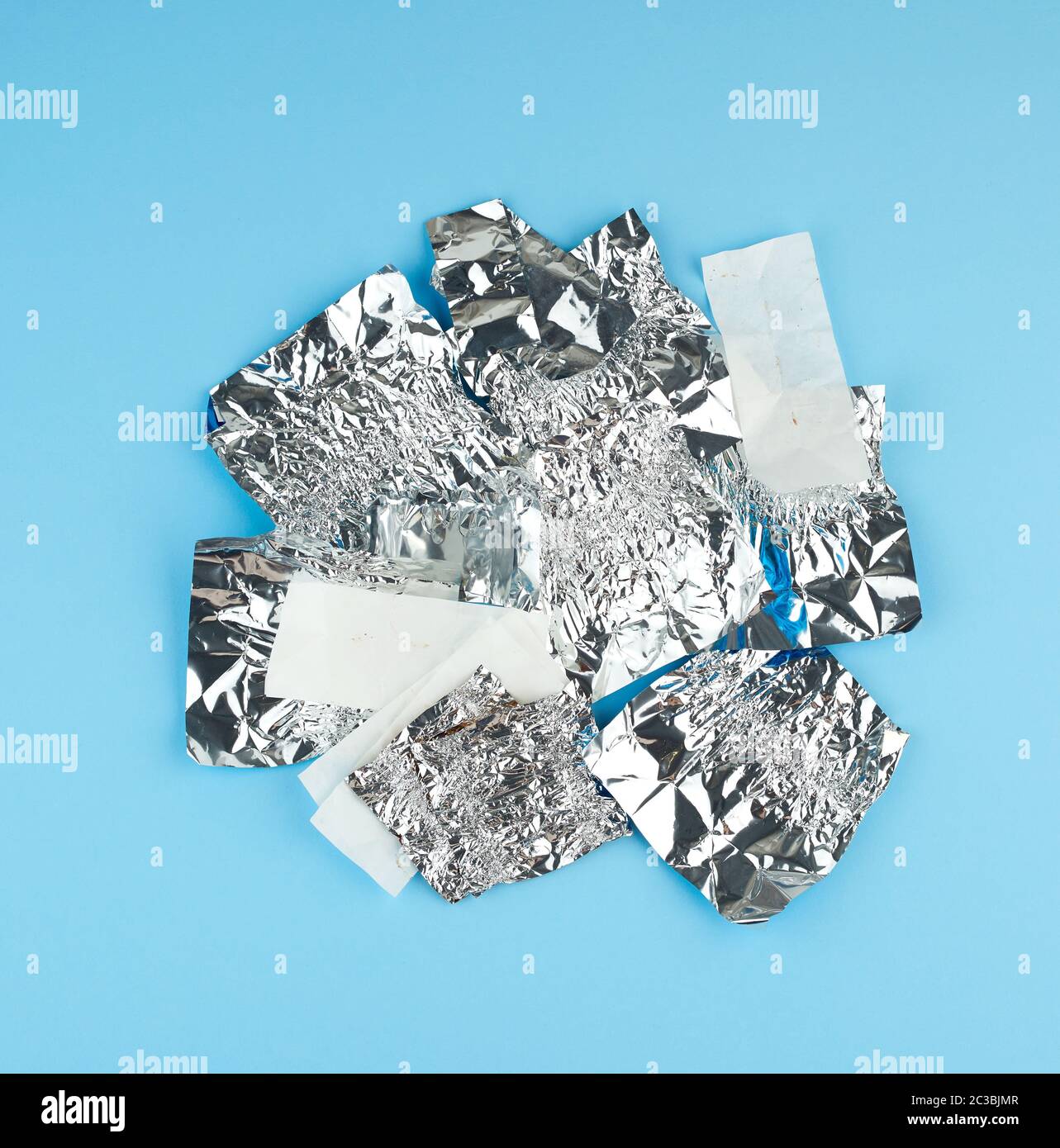 various crumpled white paper and foil used candy wrappers on a blue ...