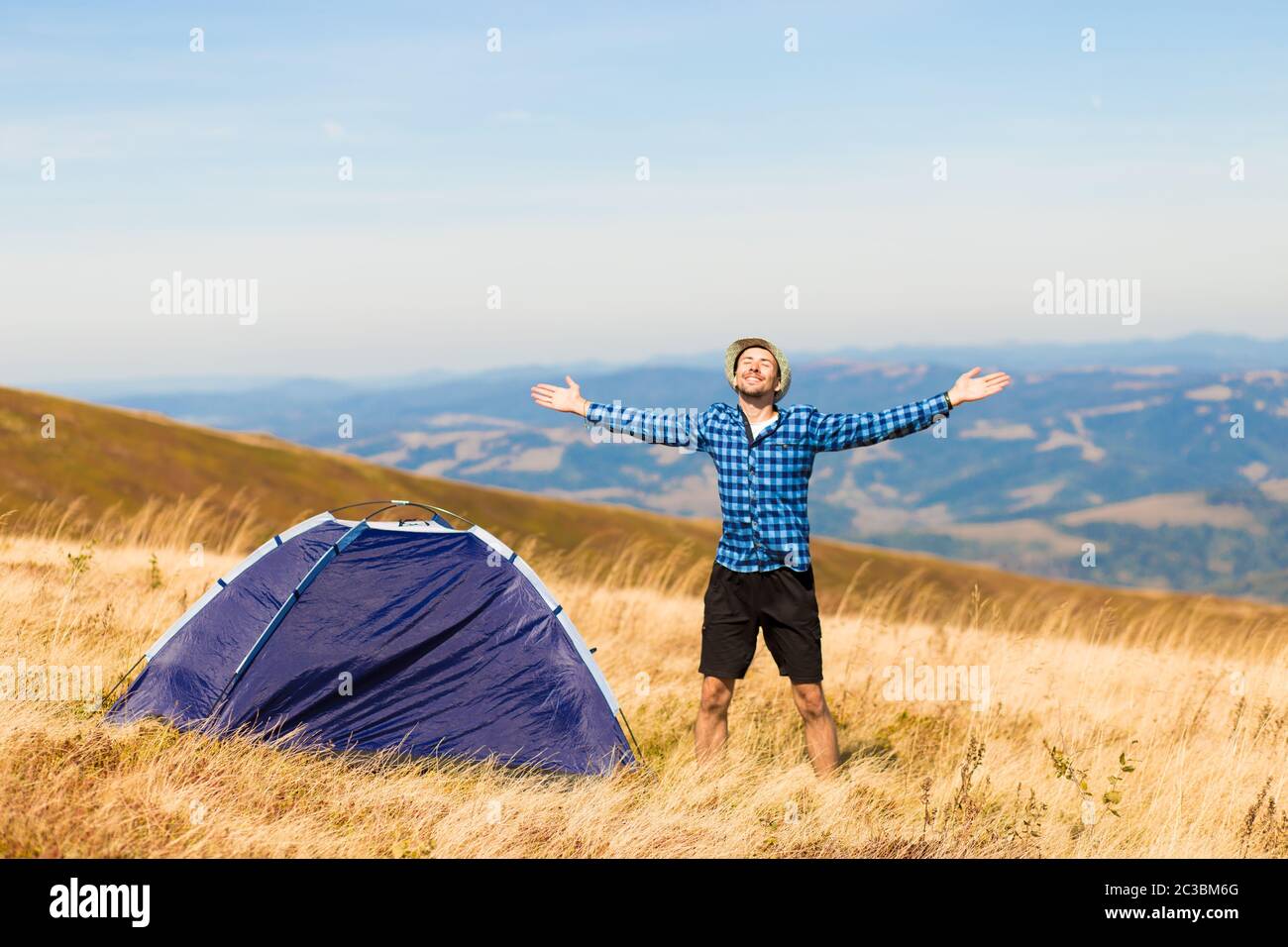 Happy traveler man on top of mountain raised hands enjoying freedom and ...