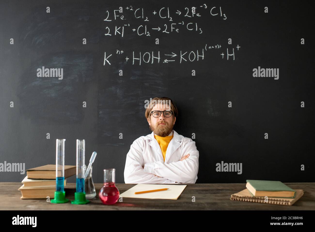 Young contemporary chemistry teacher in whitecoat crossing his arms on ...