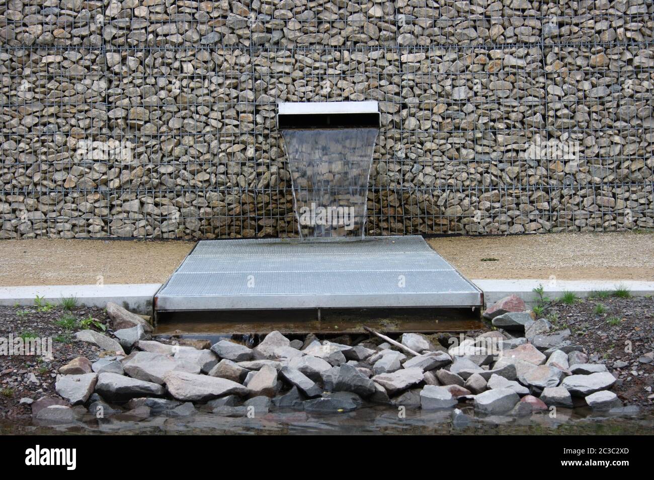 A stone wall built with gabions, from which water flows from Stock ...
