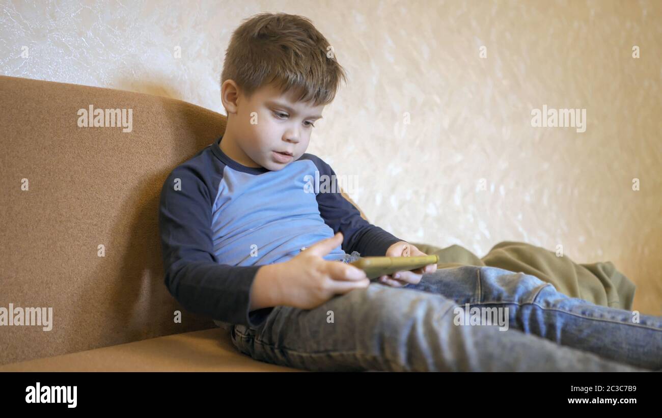 Boring boy uses cellphone while sitting alone at home on the couch ...