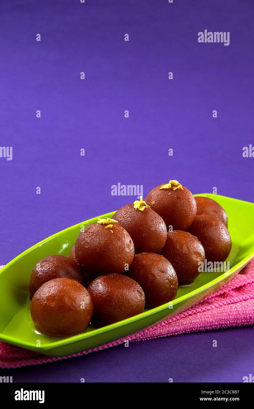 Indian Dessert Gulab Jamun in plate on purple background with napkin ...