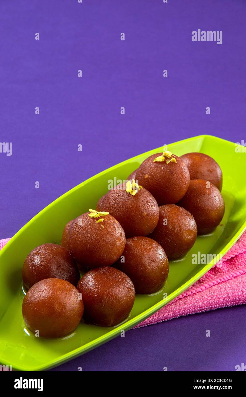 Indian Dessert Gulab Jamun in plate on purple background with napkin ...