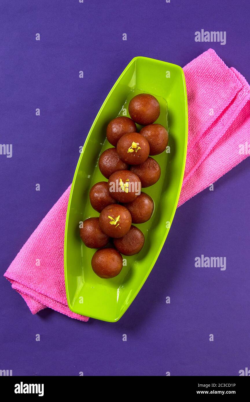Indian Dessert Gulab Jamun in plate on purple background with napkin ...