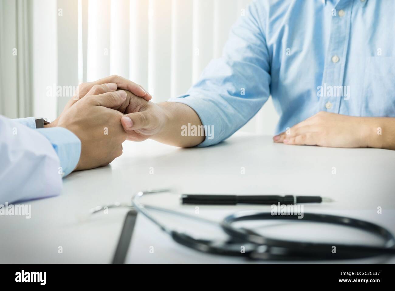 male doctor holding patient's hand, comforting patient who is in ...