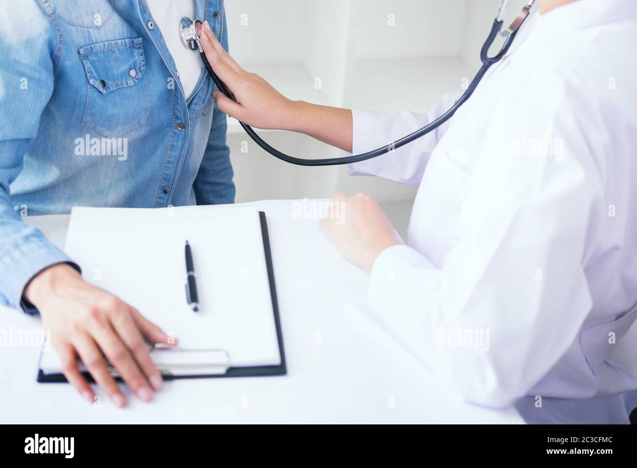 Doctor listening to cheerful young patients chest with stethoscope in ...