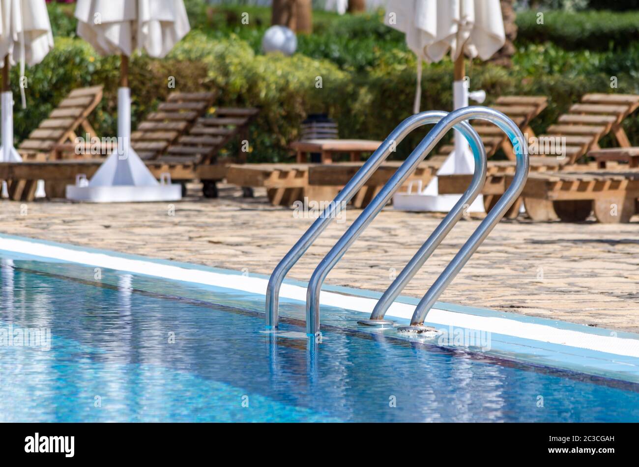 handrails by the pool with blue water against the sun loungers and ...