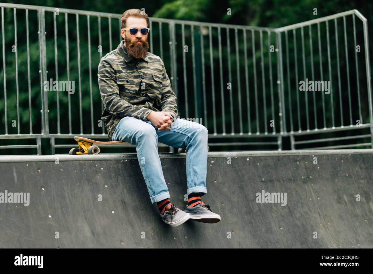 Portrait of bearded man smiling at camera while sitting on ramp in ...
