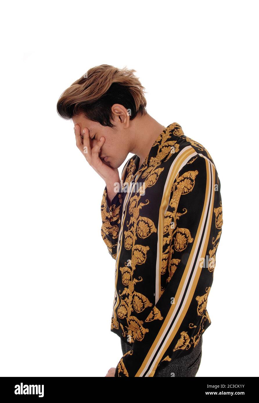 A young sad looking man standing in profile with his hand over his face ...