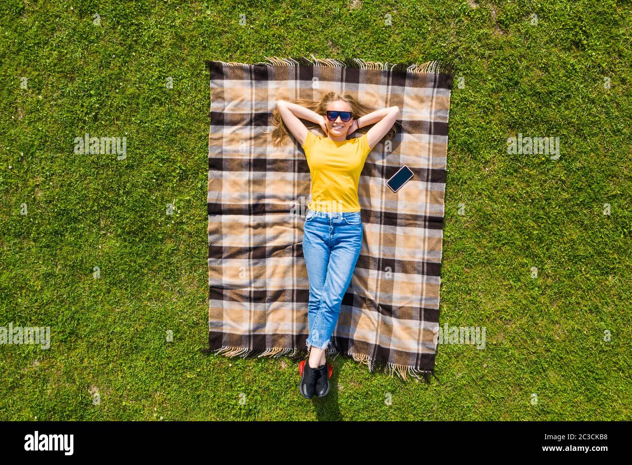 Aerial view of young woman lying on her back on the plaid towel and ...