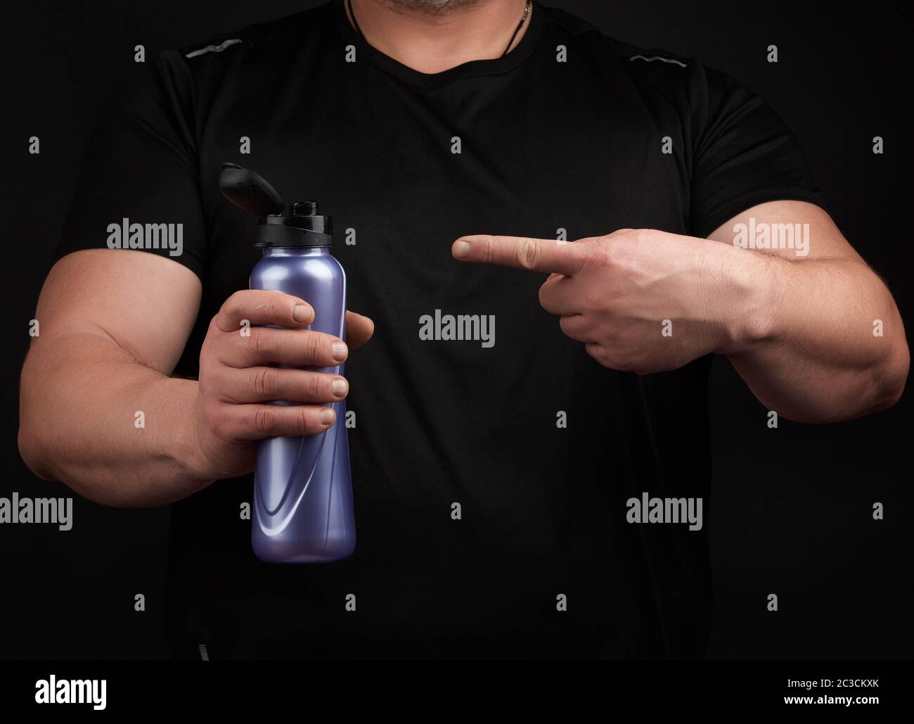 adult male athlete with muscles holds a plastic bottle of water ...