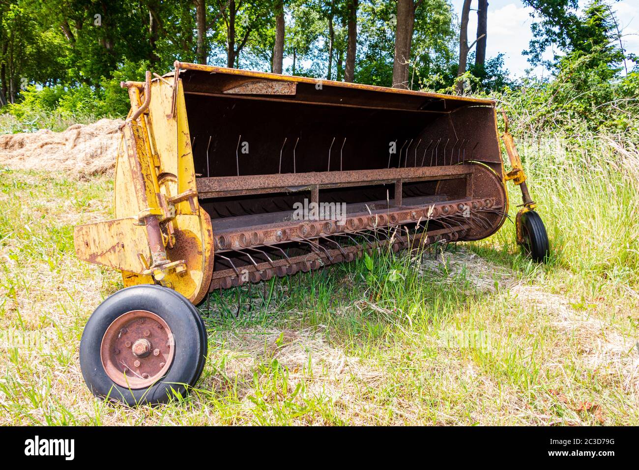 Vintage and old-fashioned yellow-painted hay tedder on land, partly ...