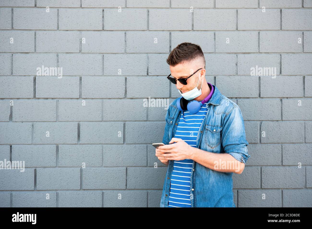Young man with headphones around his neck and lowered surgical mask ...
