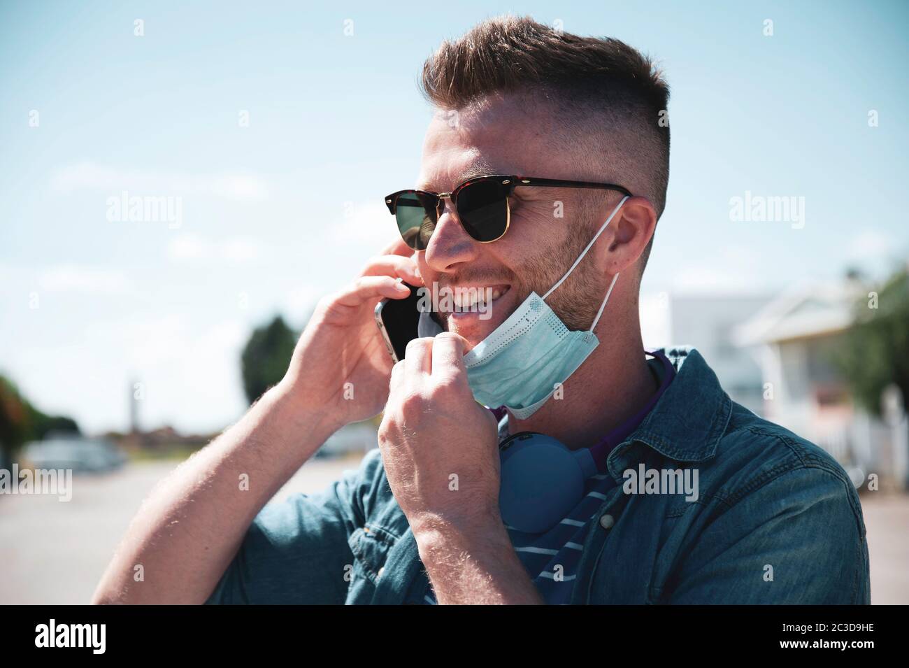Smiling man with headphones around his neck and lowered surgical mask ...