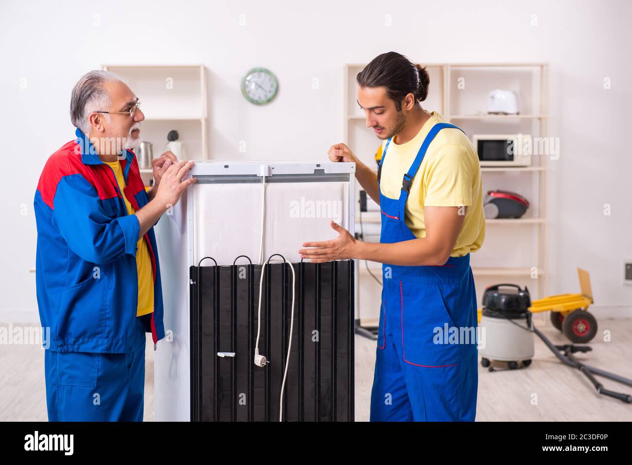 Two contractors repairing fridge at workshop Stock Photo - Alamy