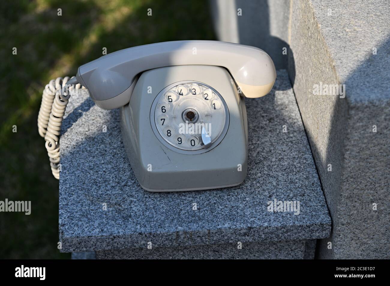 Old fashion grey rotary dial phone on granite stone pedestal outdoor ...