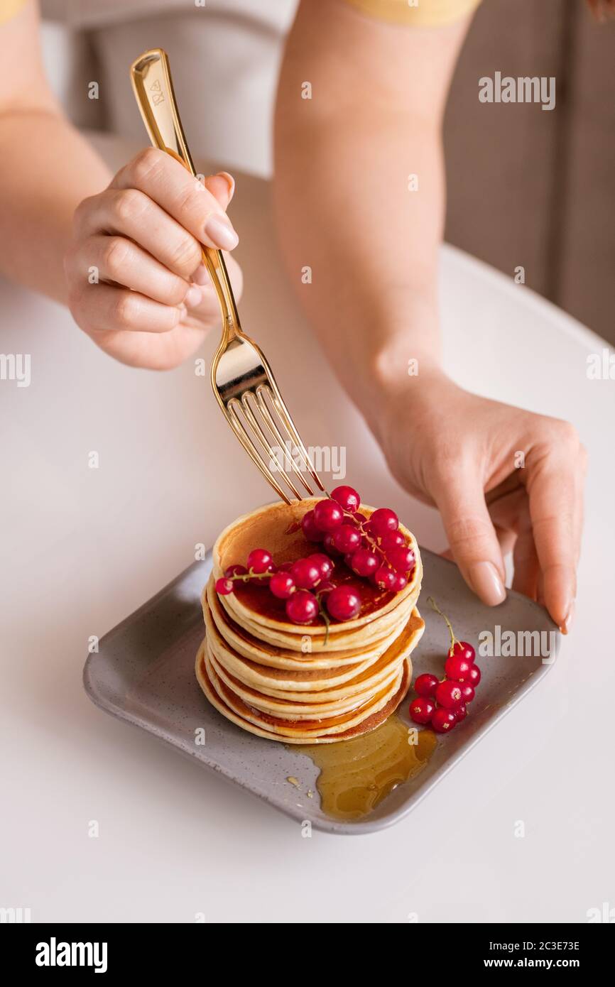 Young woman with fork bending over table while taking fresh red currant ...