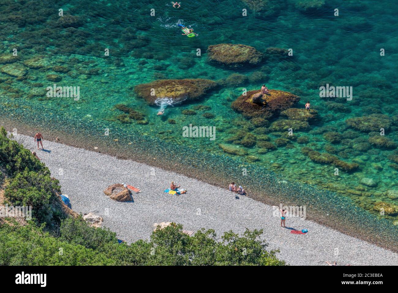 People sunbathe and swim on the pebble beach. Untouched nature, clean ...