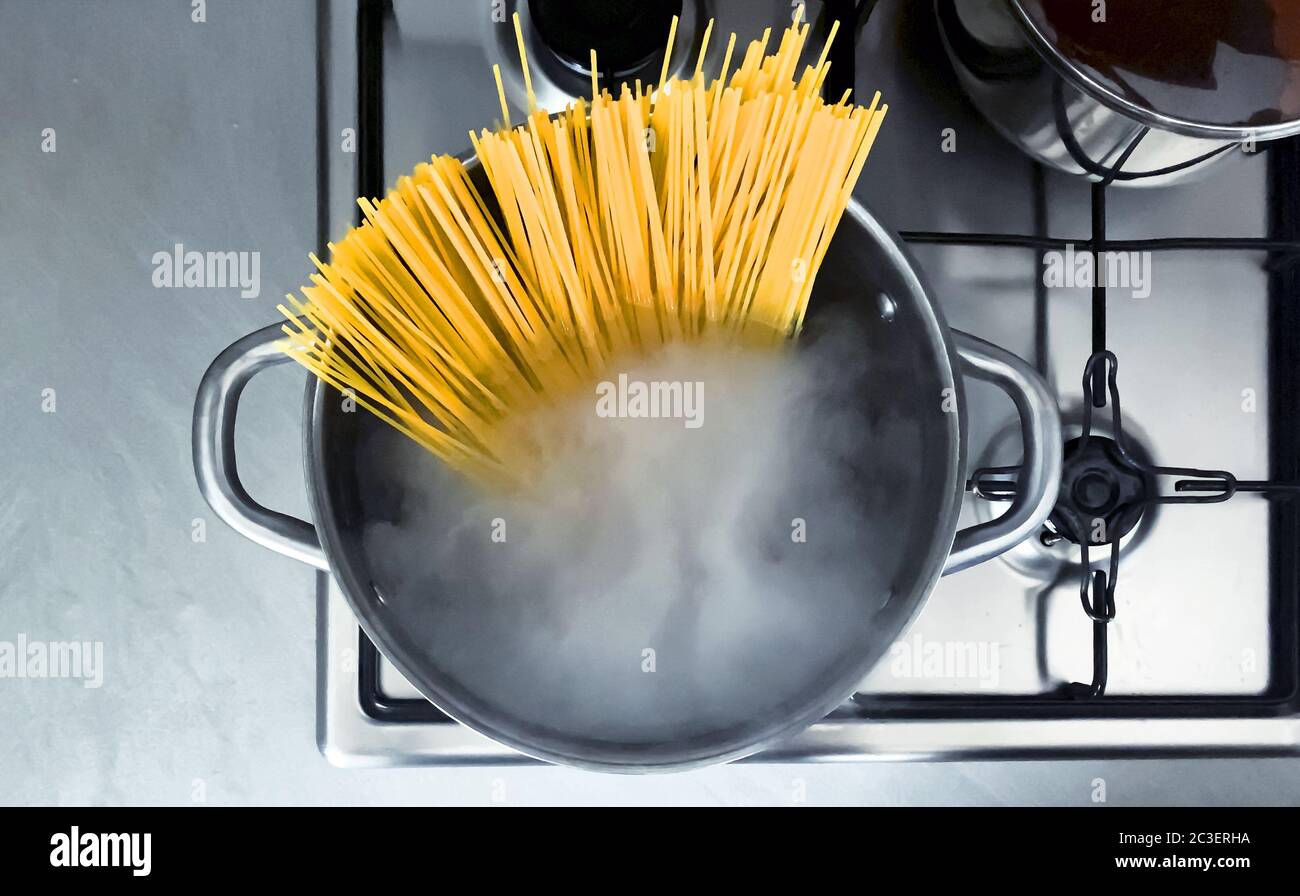 Cooking raw spaghetti in the boiling water contained in a saucepan ...