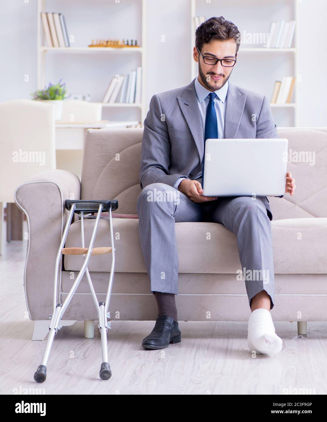 Businessman with crutches and broken leg at home working Stock Photo ...