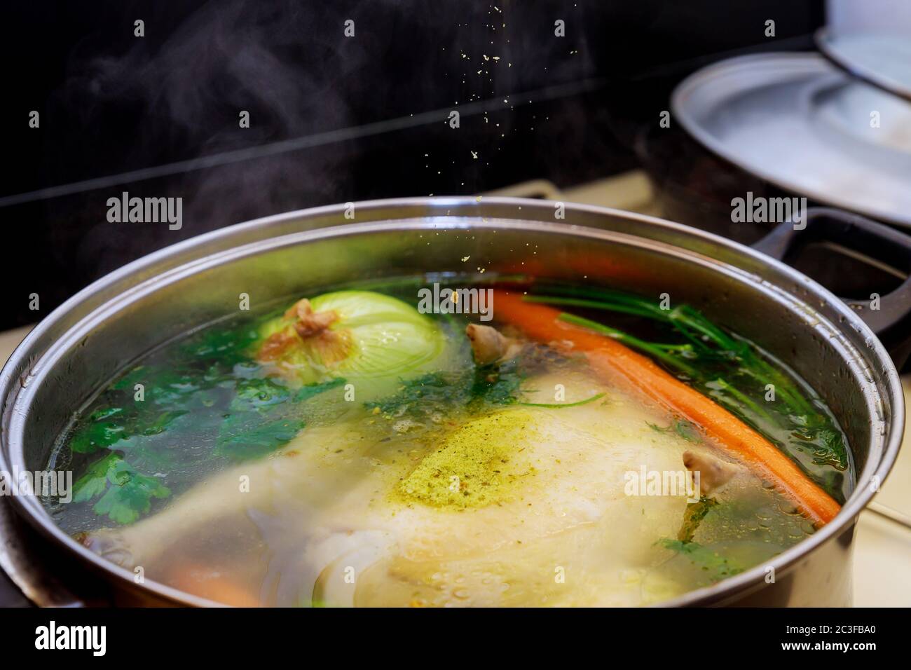 Pouring seasoning into boiling chicken broth with vegetables in steel ...