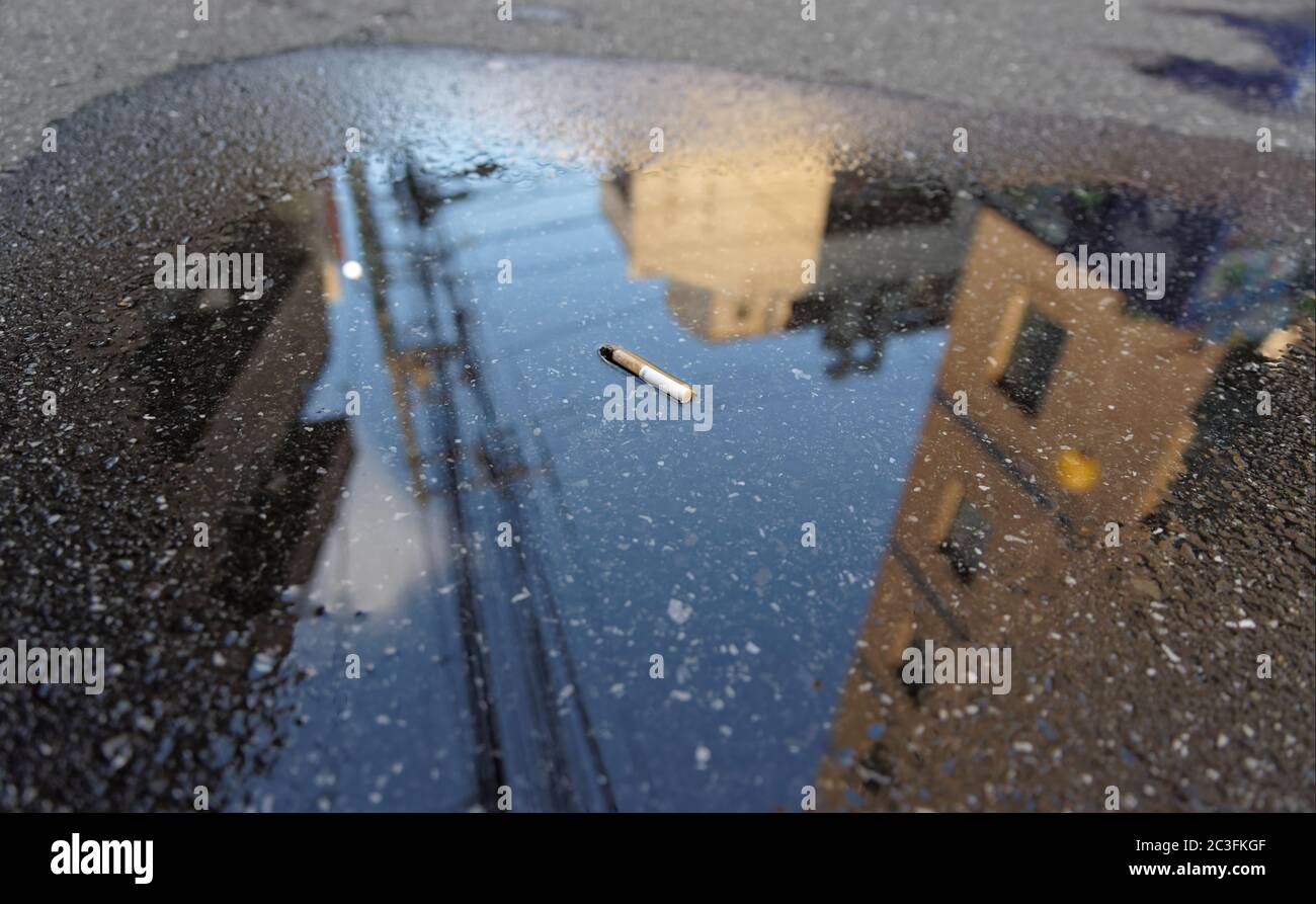 Partly-smoked cigarette sitting in a puddle on a city street ...