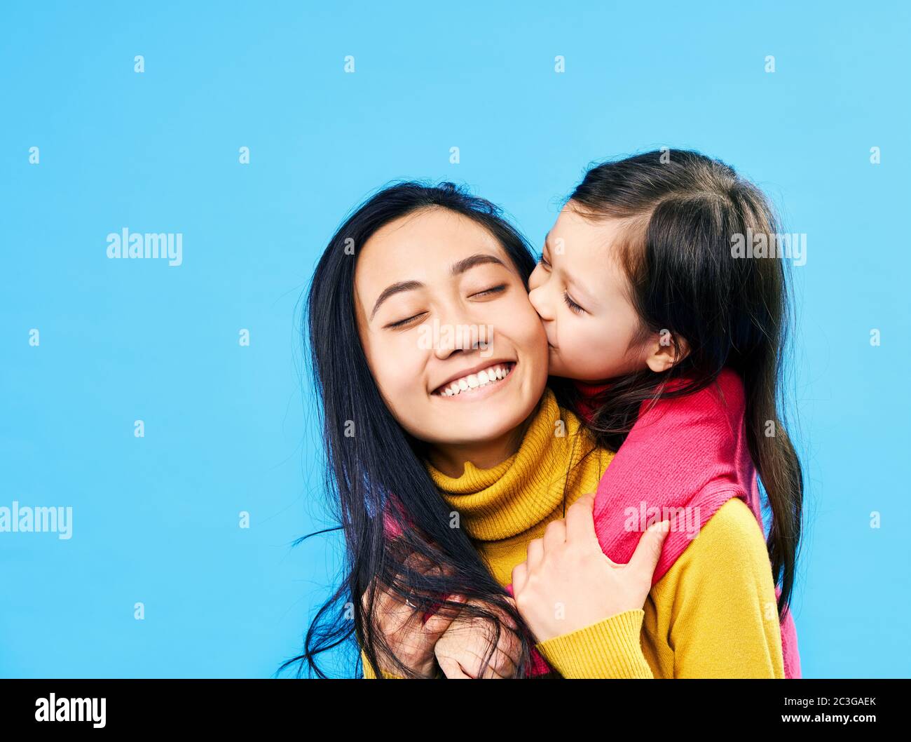 Little cute daughter hug and kissing her happy mother isolated on blue ...