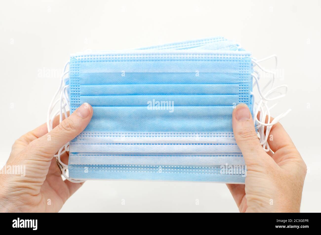 Two hands holding several disposable surgical face masks to cover the ...