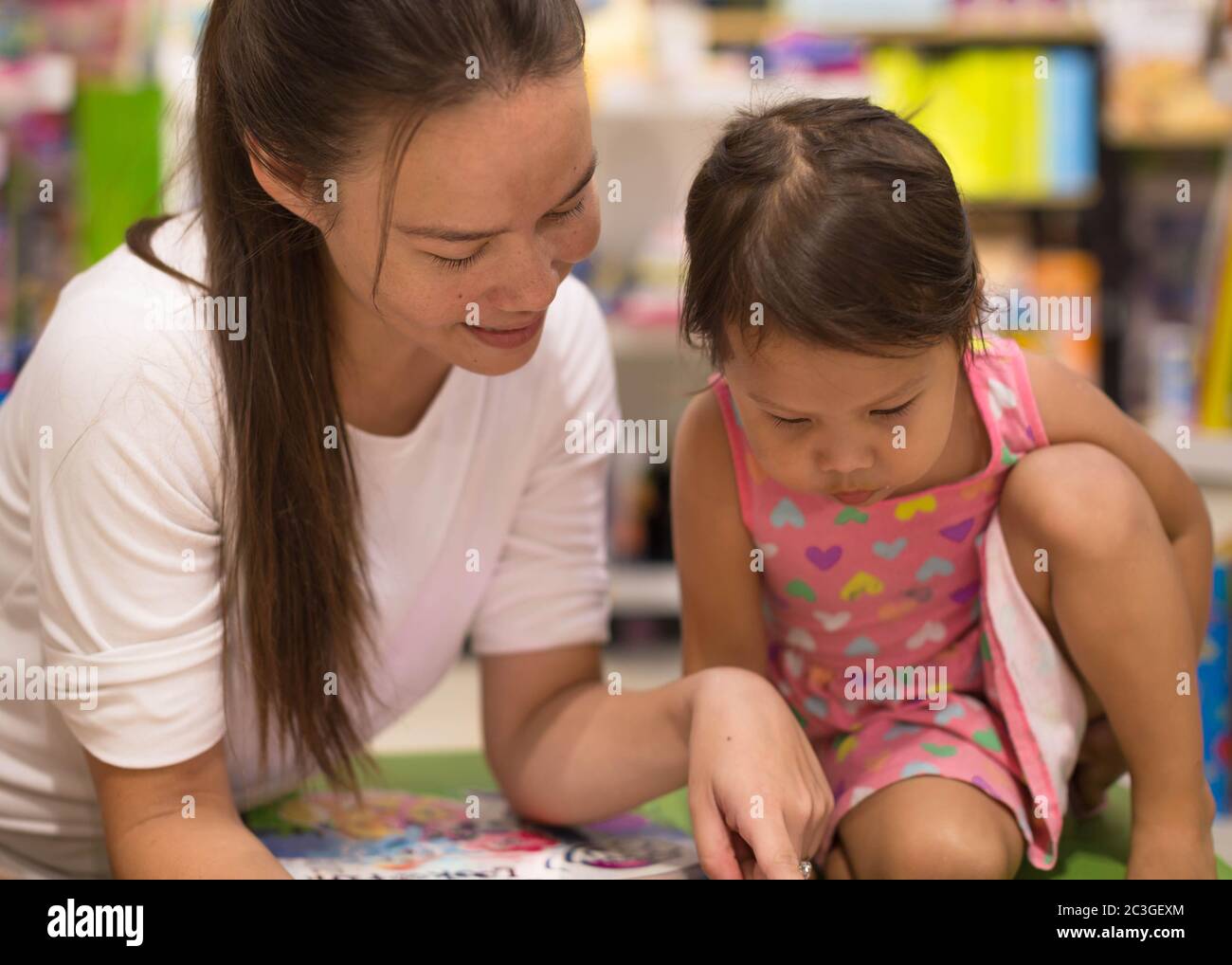 Mother is happily teaching her daughter how to read in a library. High ...