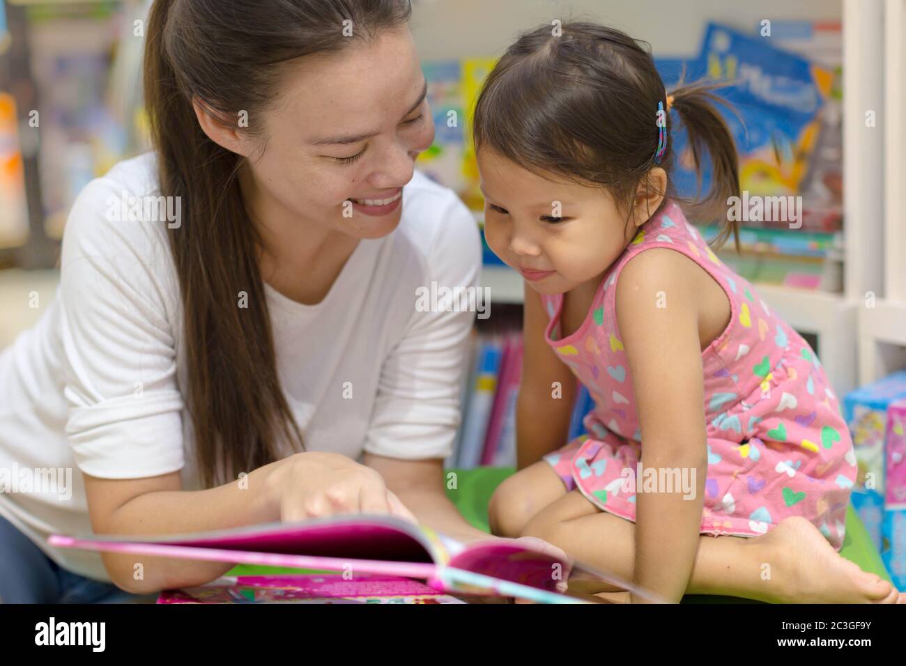 Mother is happily teaching her daughter how to read in a library. High ...