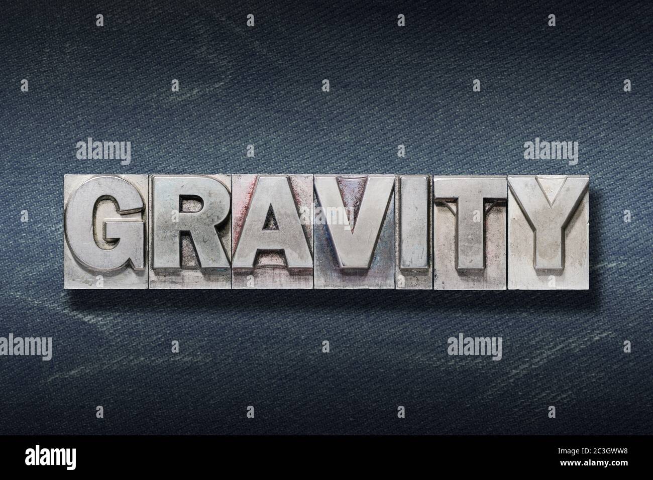 gravity word made from metallic letterpress on dark jeans background ...